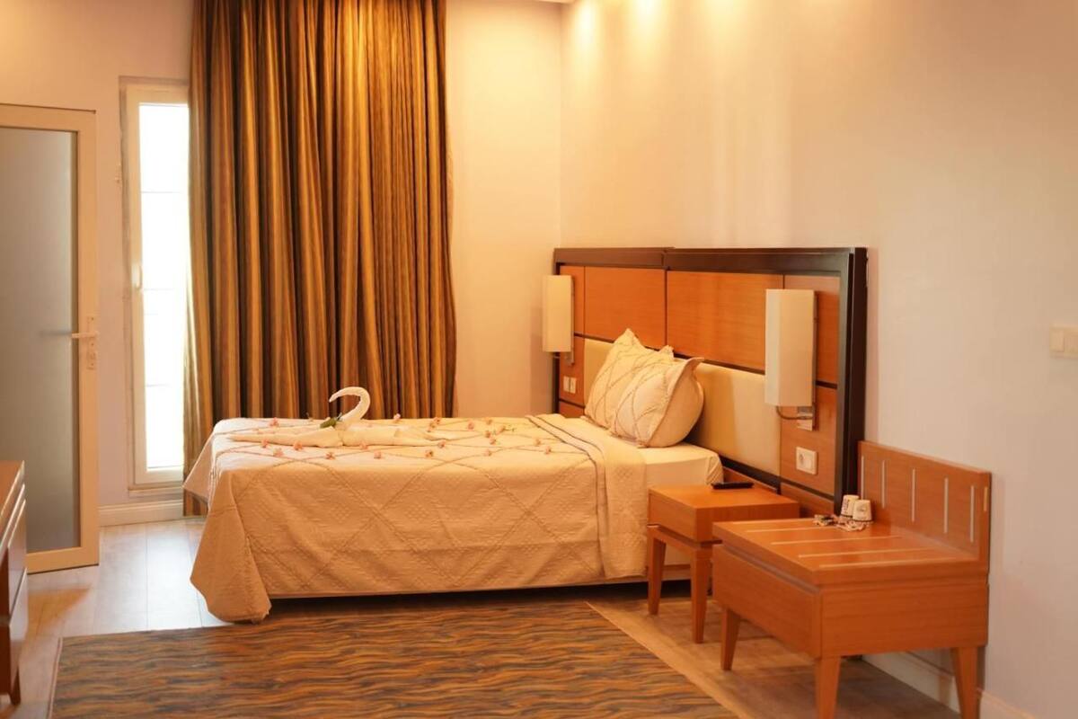 Quarto de hotel com cama, mesa de cabeceira e uma pequena cadeira de madeira.