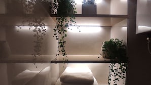 Casa de banho com toalhas empilhadas a branco, uma planta pendente e uma estante com um vaso de planta.