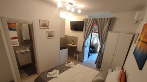 Quarto de hotel com cama, escrivaninha, cadeira, televisão e guarda-roupa.