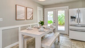 Uma cozinha com geladeira branca, uma mesa de jantar com bancos e duas fotos emolduradas na parede.
