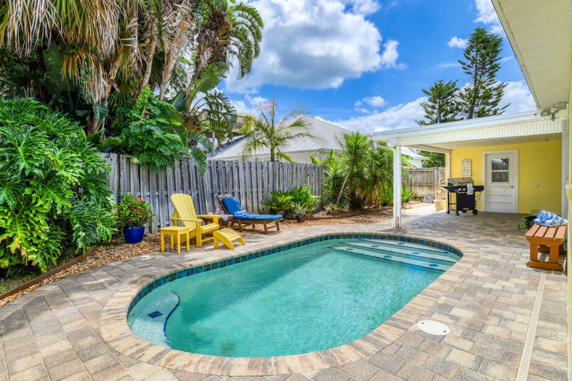 Um quintal com piscina, deck de madeira e área de varanda coberta.