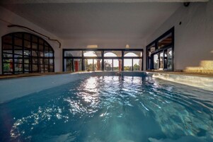 Piscina interior com água cristalina, grandes janelas e vista para o exterior.