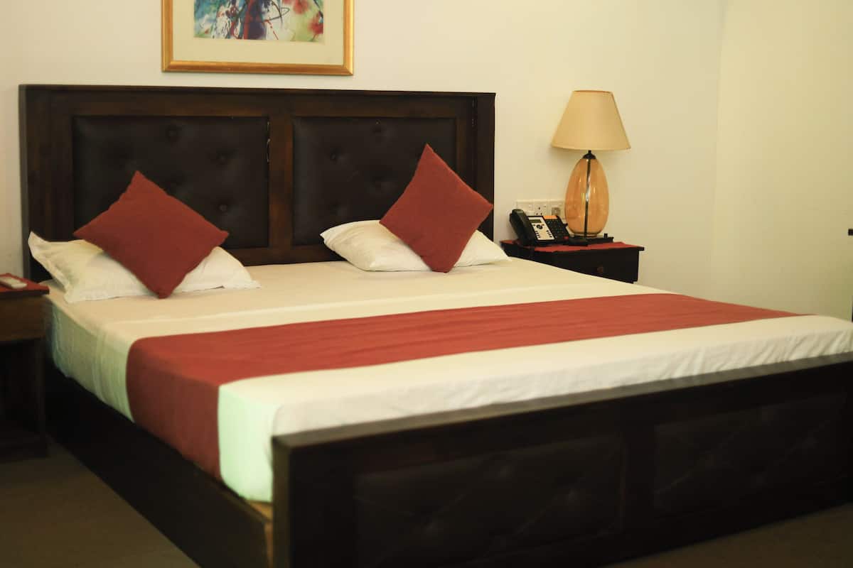 Quarto de hotel com uma cama grande, duas almofadas, uma mesa de cabeceira com abajur e um quadro na parede.