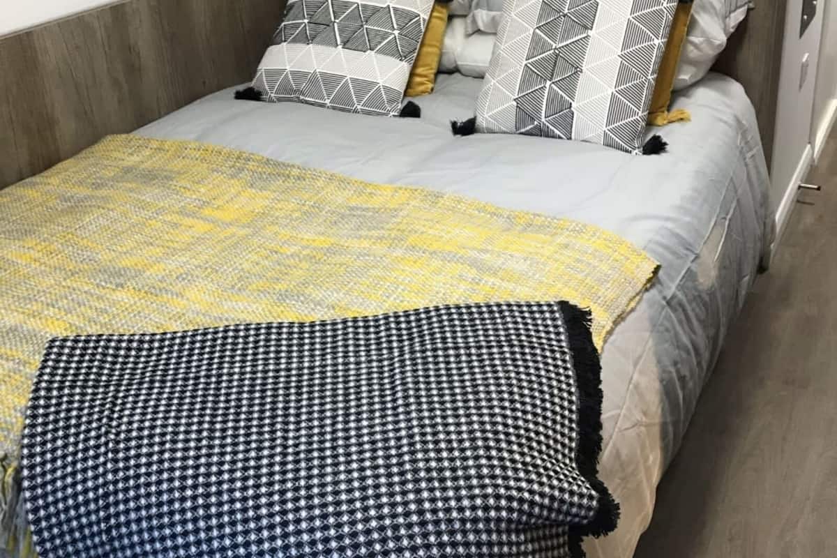 Uma cama com travesseiro estampado em padrão geométrico, um cobertor amarelo e um cobertor xadrez.