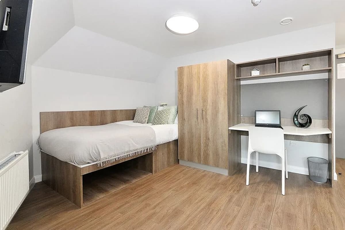 Quarto compacto com uma cama, escrivaninha e computador.