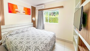 Quarto moderno com uma cama grande, televisão de tela plana, ar condicionado e janela com cortinas.