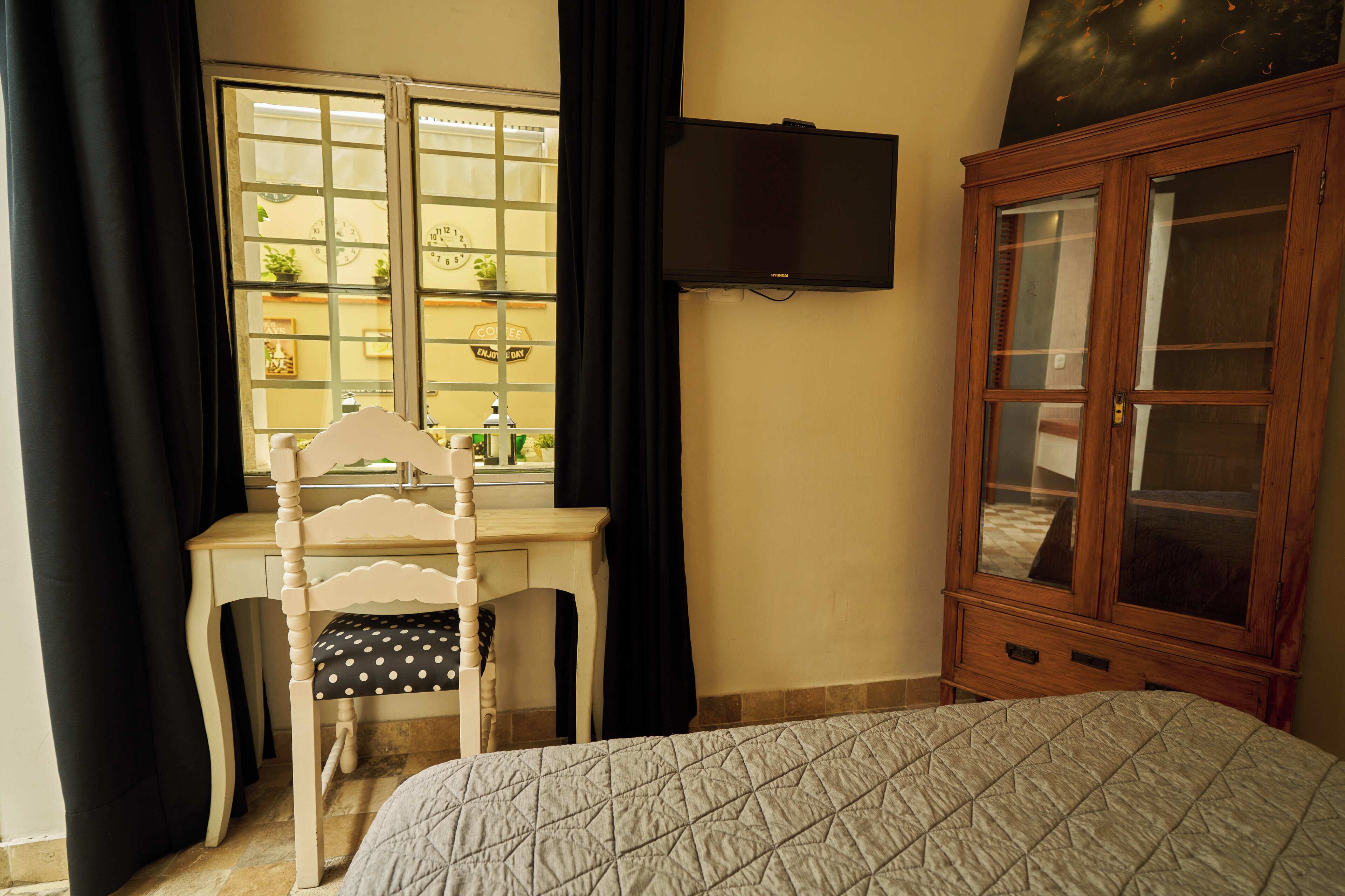 Quarto com cama, escrivaninha com cadeira, televisão e armário.