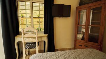 Quarto com cama, escrivaninha com cadeira, televisão e armário.