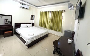 Quarto de hotel com cama, escrivaninha, cadeira, televisão e janela com cortinas.