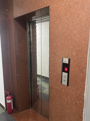 Um elevador com painel de controle, extintor de incêndio e parede com quadro de cortiça.