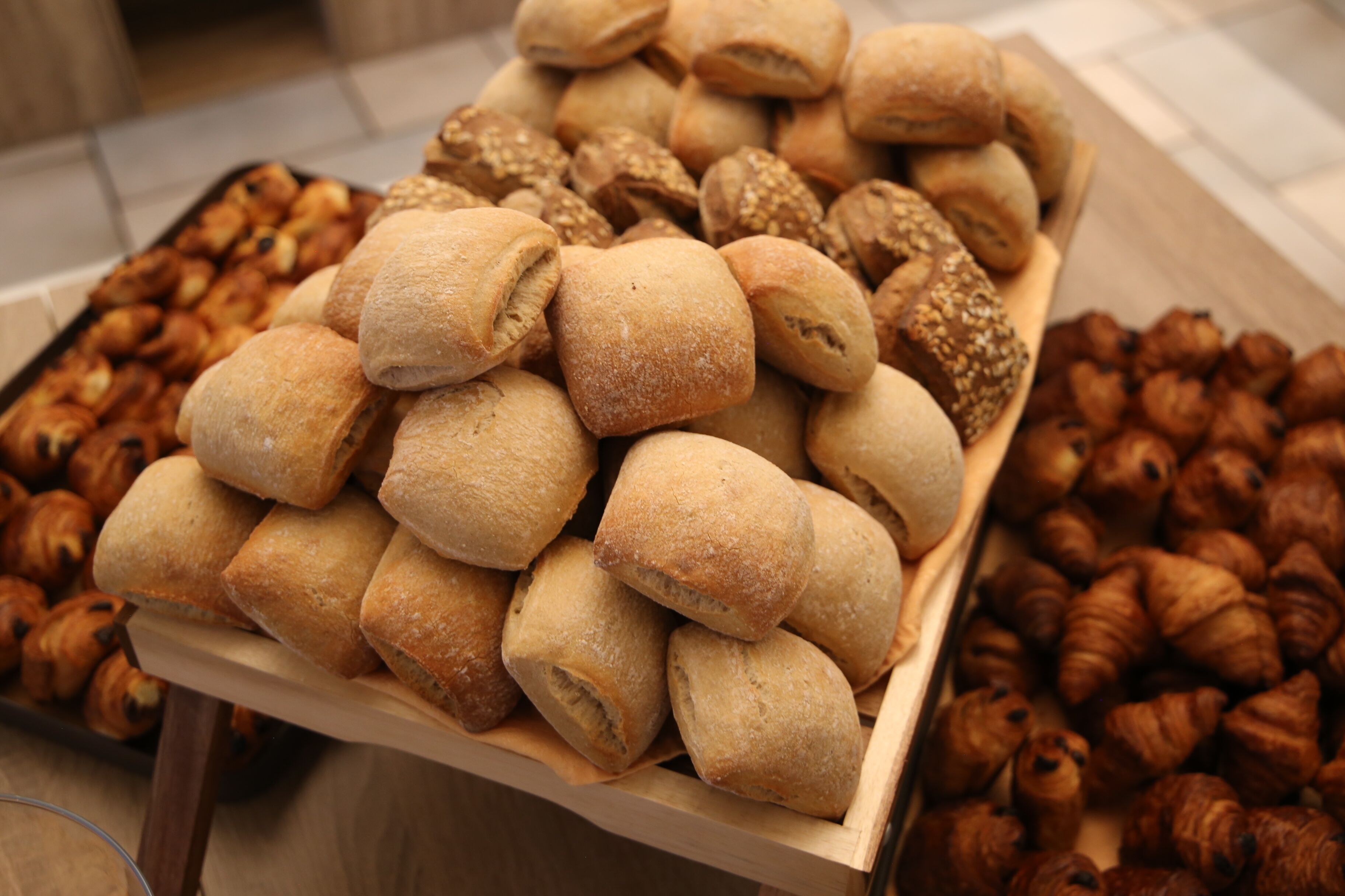Diversos produtos de panificação, incluindo pães e croissants, expostos em uma tábua de madeira.