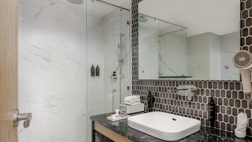 Uma casa de banho moderna com chuveiro de mármore, um espelho grande e uma pia branca.