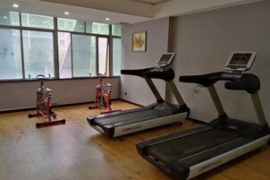 Academia com esteiras e bicicletas ergométricas, janelas amplas e piso de madeira.