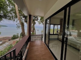 Varanda com vista para o mar, piso de madeira e porta de vidro que dá para um quarto.