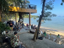 Um café à beira-mar com mesas ao ar livre, um deck de madeira e vista para o mar.