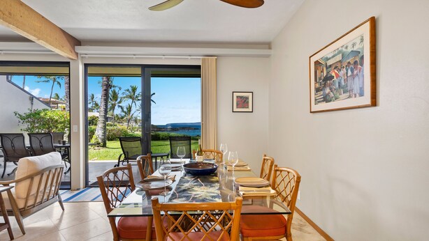 Área de refeições com mesa posta para quatro pessoas, com vista panorâmica para palmeiras e um corpo d'água.