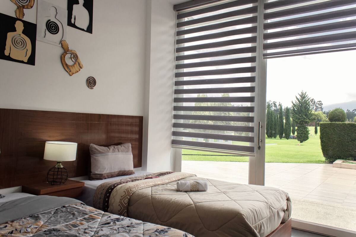 Um quarto com cama, mesa de cabeceira, abajur e janela com persianas.