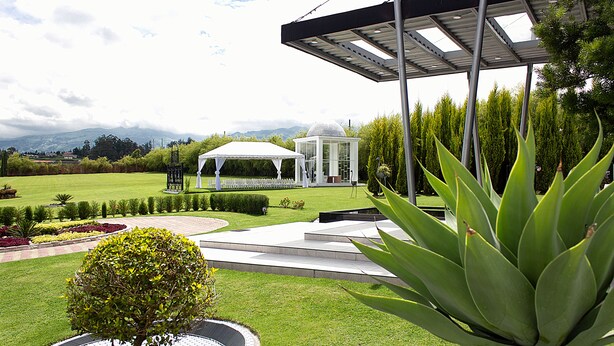Um jardim bem cuidado com um gazebo, um espelho d'água circular e uma grande planta de agave.