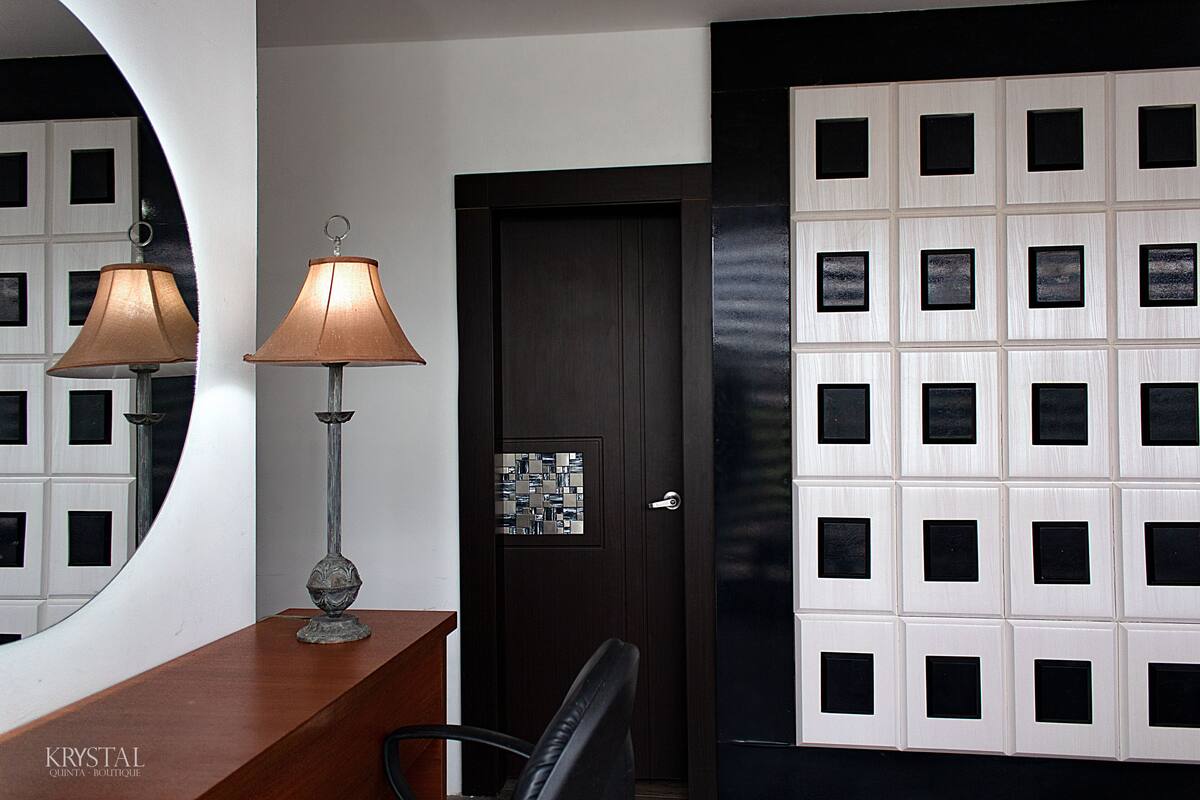 Um quarto com uma escrivaninha de madeira, duas luminárias, um espelho e uma porta com painel de vidro estampado.