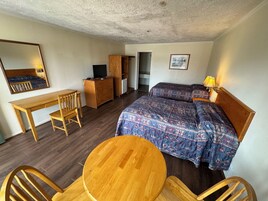 Quarto de hotel com escrivaninha de madeira, duas camas com roupa de cama estampada, uma televisão, um guarda-roupa e uma mesinha.