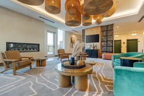 Um lobby moderno com uma mesa de vidro redonda, cadeiras de vime, um sofá azul-turquesa e um papel de parede estampado.