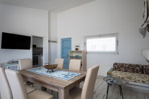Uma área de refeições com uma mesa de madeira, cadeiras e uma TV fixada na parede.