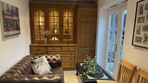 Uma sala de estar com um sofá de couro marrom, uma mesa de centro de madeira e uma cadeira de madeira. Ao fundo, um armário grande com portas de vidro.