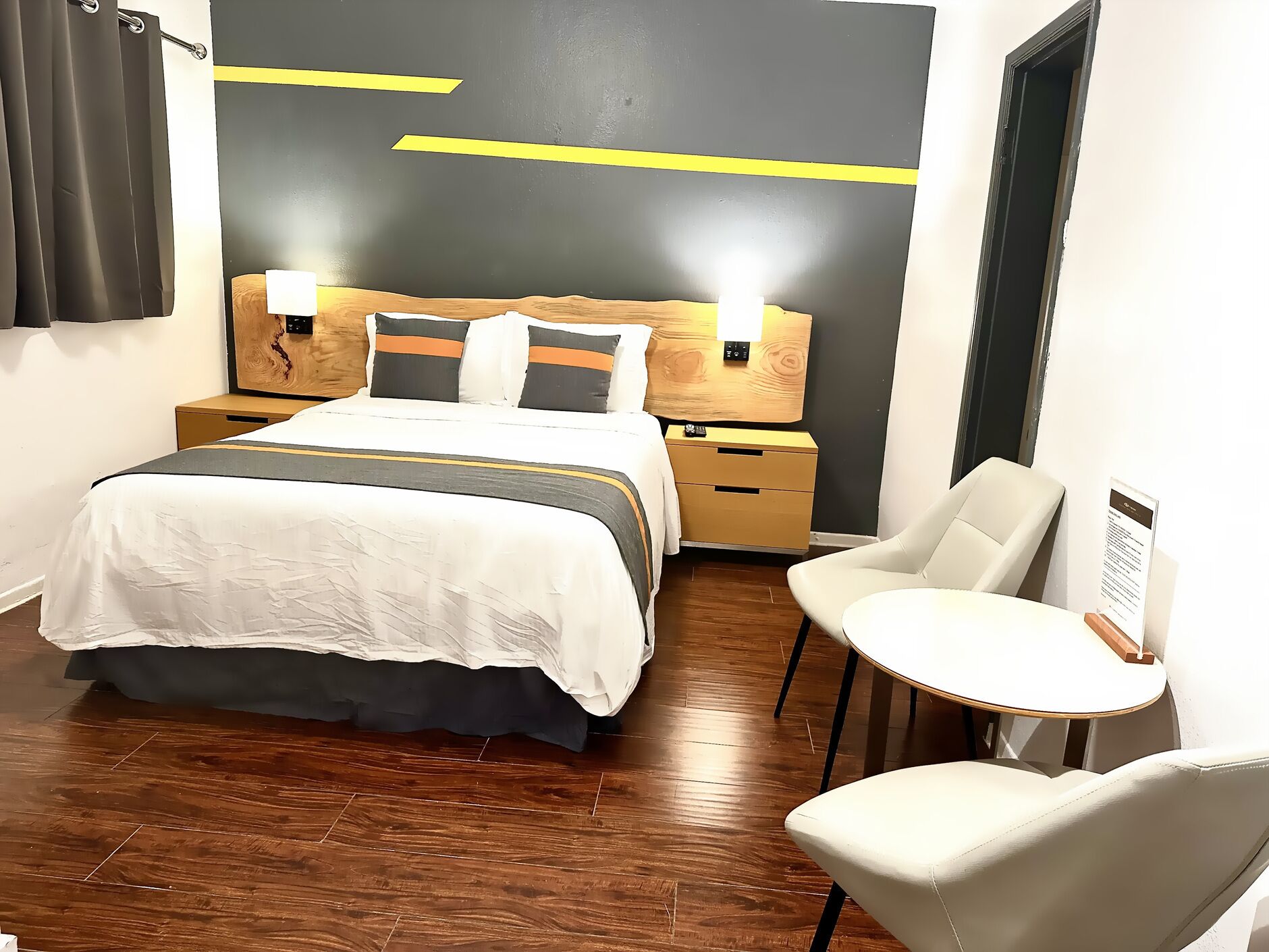 Quarto de hotel com cama, mesas de cabeceira, uma cadeira e uma pequena mesa.