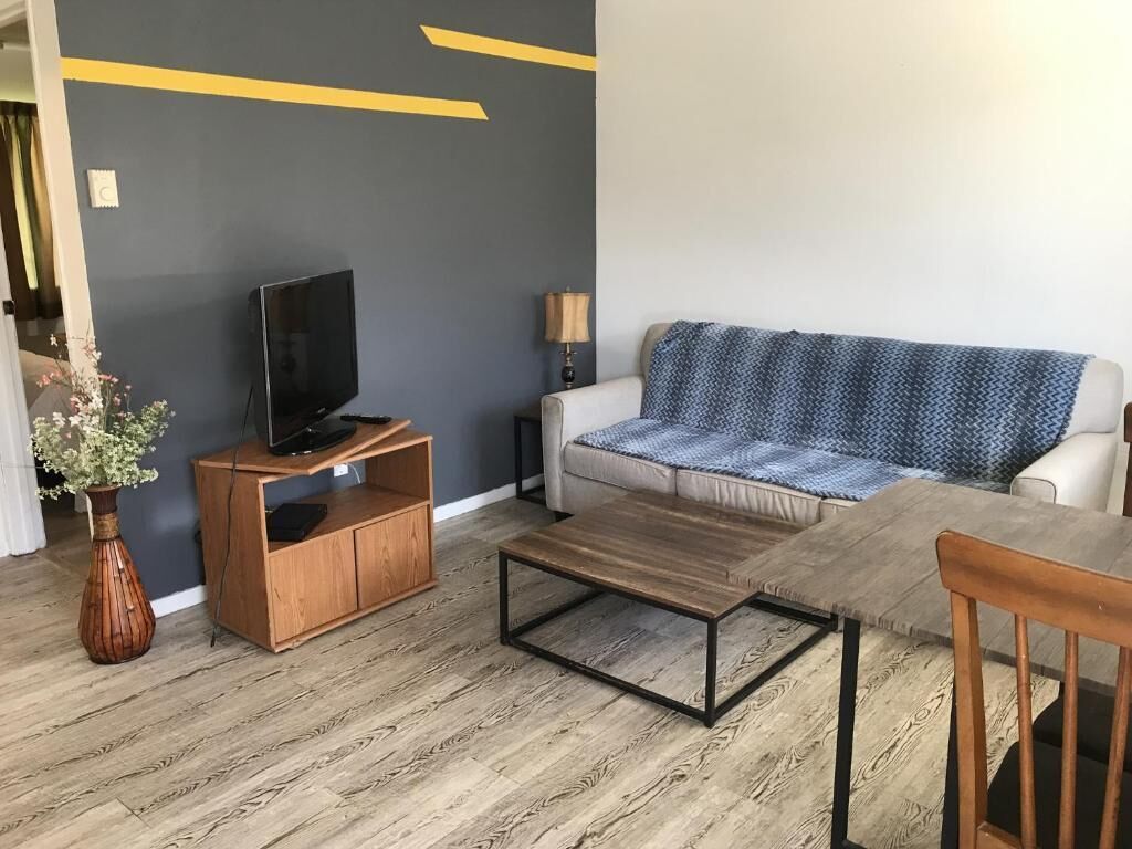 Uma sala de estar com um sofá, uma mesa de centro, uma TV em um suporte de madeira e um abajur.