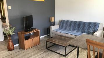 Uma sala de estar com um sofá, uma mesa de centro, uma TV em um suporte de madeira e um abajur.