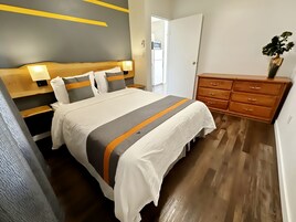 Quarto de hotel com cama, mesas de cabeceira, cômoda e porta.