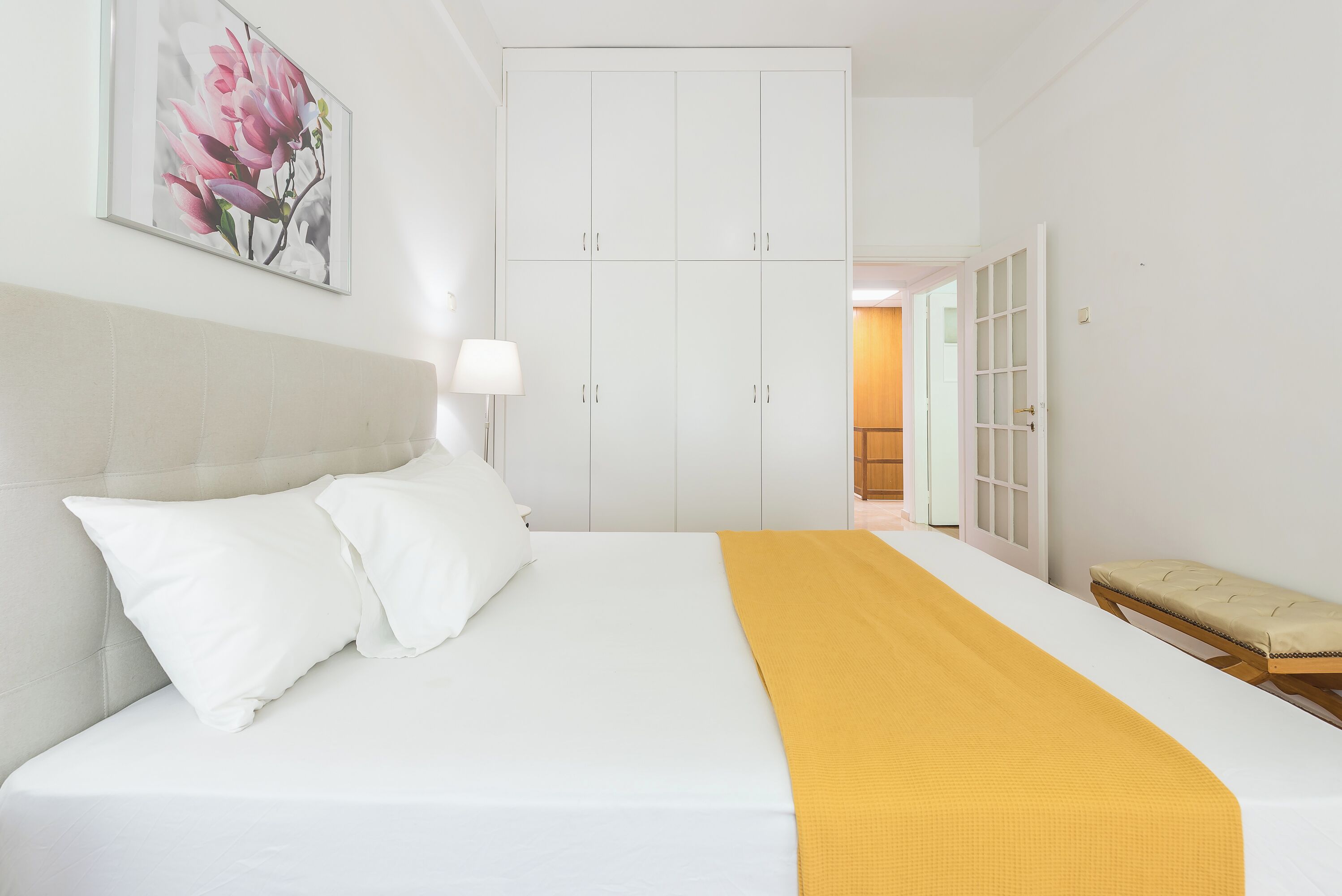 Quarto com cama, guarda-roupa branco e um banquinho.
