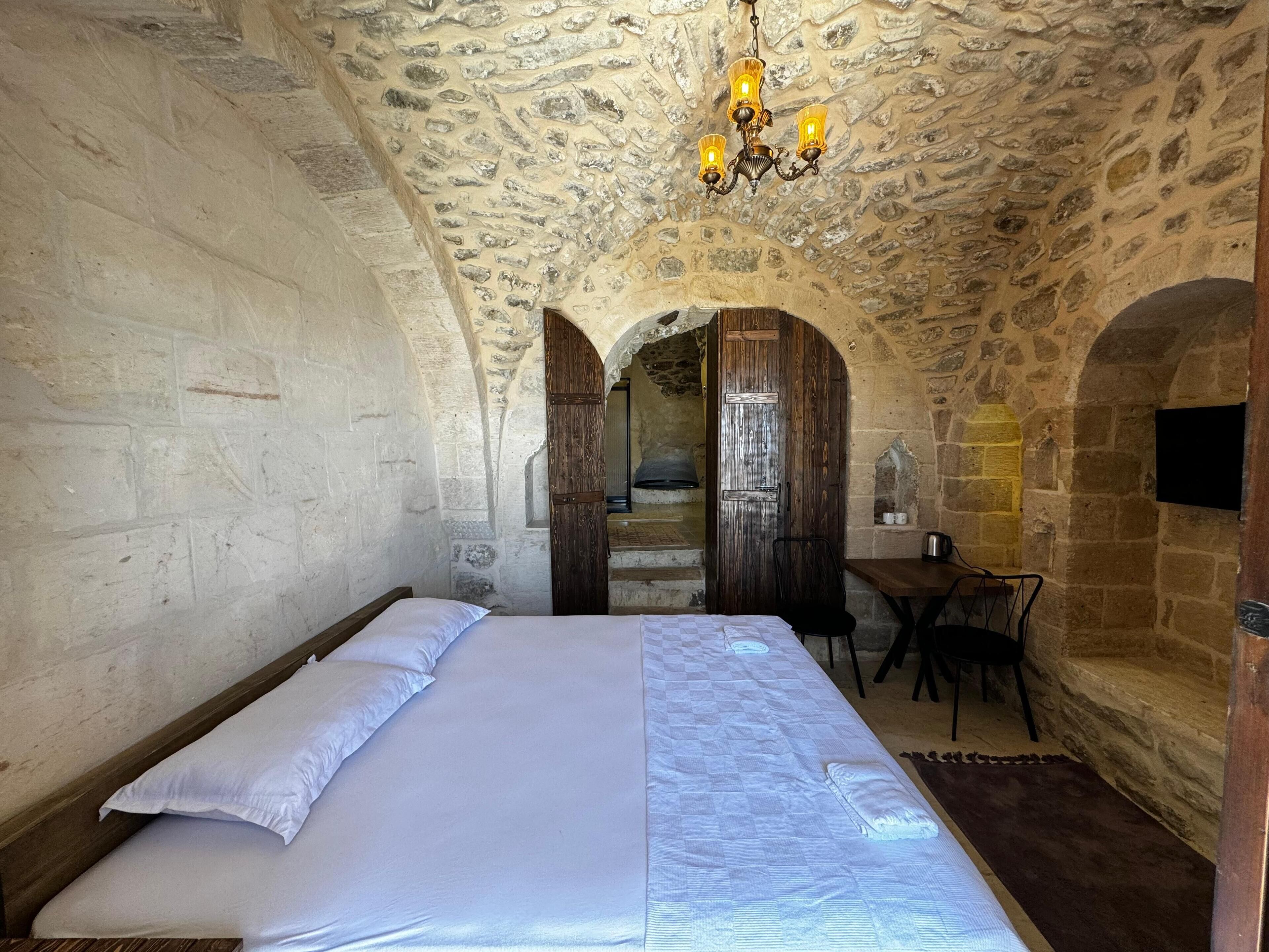 Quarto com cama, porta de madeira, parede de pedra e lustre.