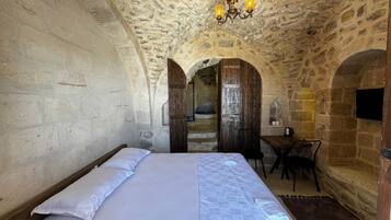 Quarto com cama, porta de madeira, parede de pedra e lustre.