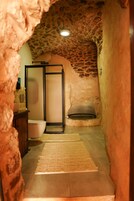 Casa de banho com paredes de pedra, vaso sanitário, lavatório e zona de duche.