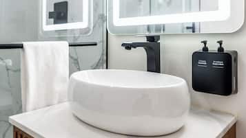 Um banheiro com pia de mármore branco, uma toalha pendurada em uma barra de toalhas preta e um espelho com iluminação embutida.