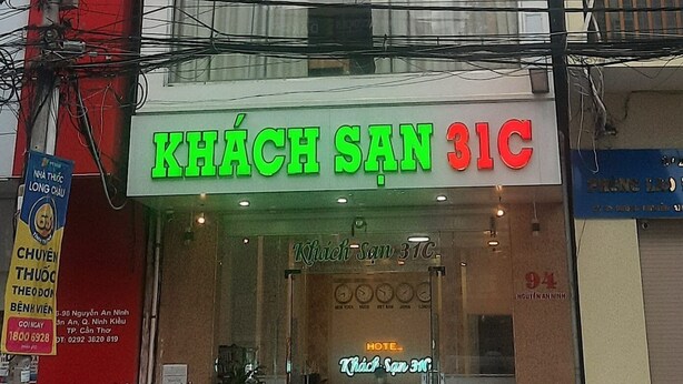 Hotel chamado "KHÁCH SAN 31C", com entrada visível, área externa com mesas e cadeiras, e placa anunciando atrações próximas.