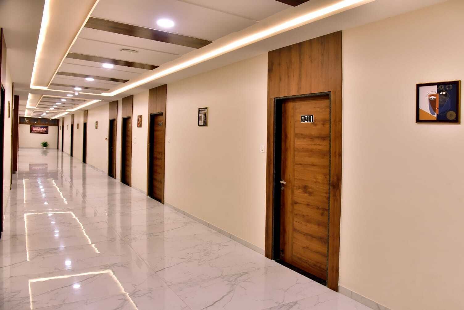 Um corredor de hotel com chão de mármore polido, portas de madeira e um design moderno no teto.