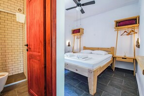 Quarto com cama de madeira, ventoinha no teto, mesa de cabeceira de madeira, cômoda de madeira e porta vermelha.