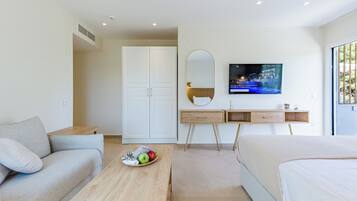 Quarto de hotel moderno com sofá, mesa de jantar com frutas, televisão, escrivaninha e guarda-roupa.