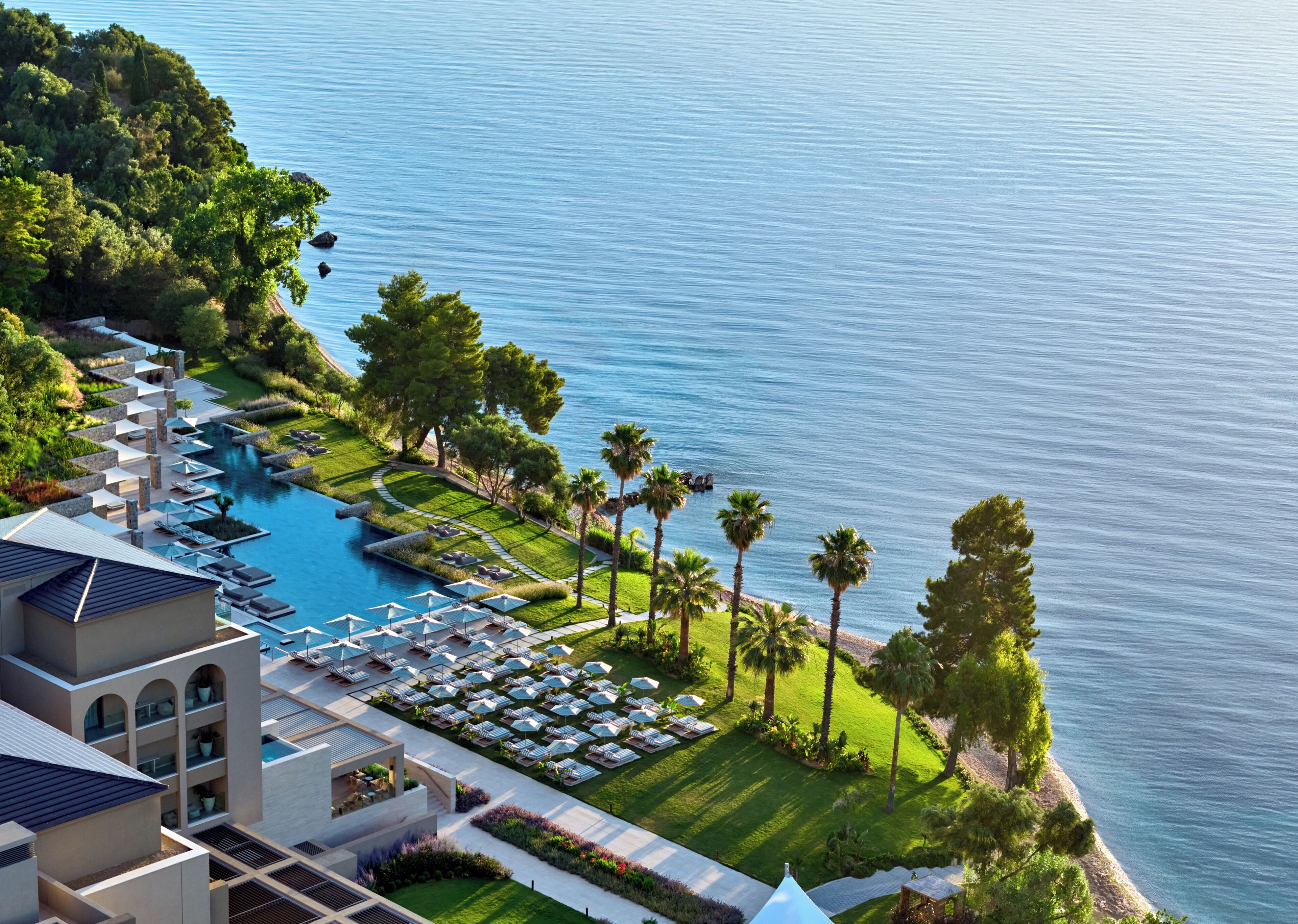 Vista aérea de um resort com piscina, áreas de descanso e vista para o mar.