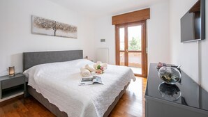 Quarto com cama, mesa de cabeceira e televisão sobre um suporte.