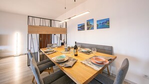 Uma sala de jantar com uma mesa de madeira posta para quatro pessoas, cercada por cadeiras estofadas cinzentas.