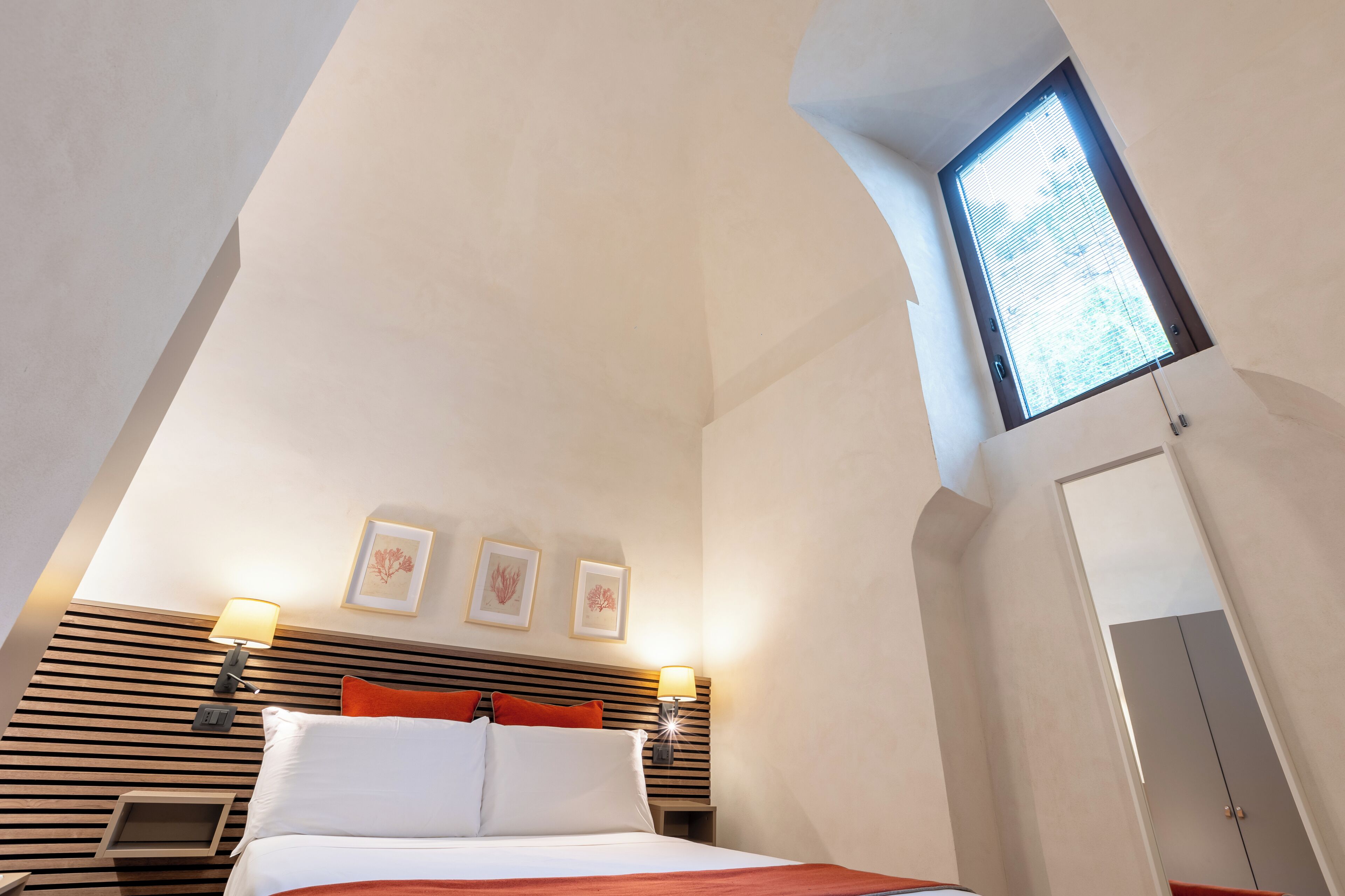 Quarto com cama, duas luminárias de cabeceira, mesa de cabeceira, janela e guarda-roupa.