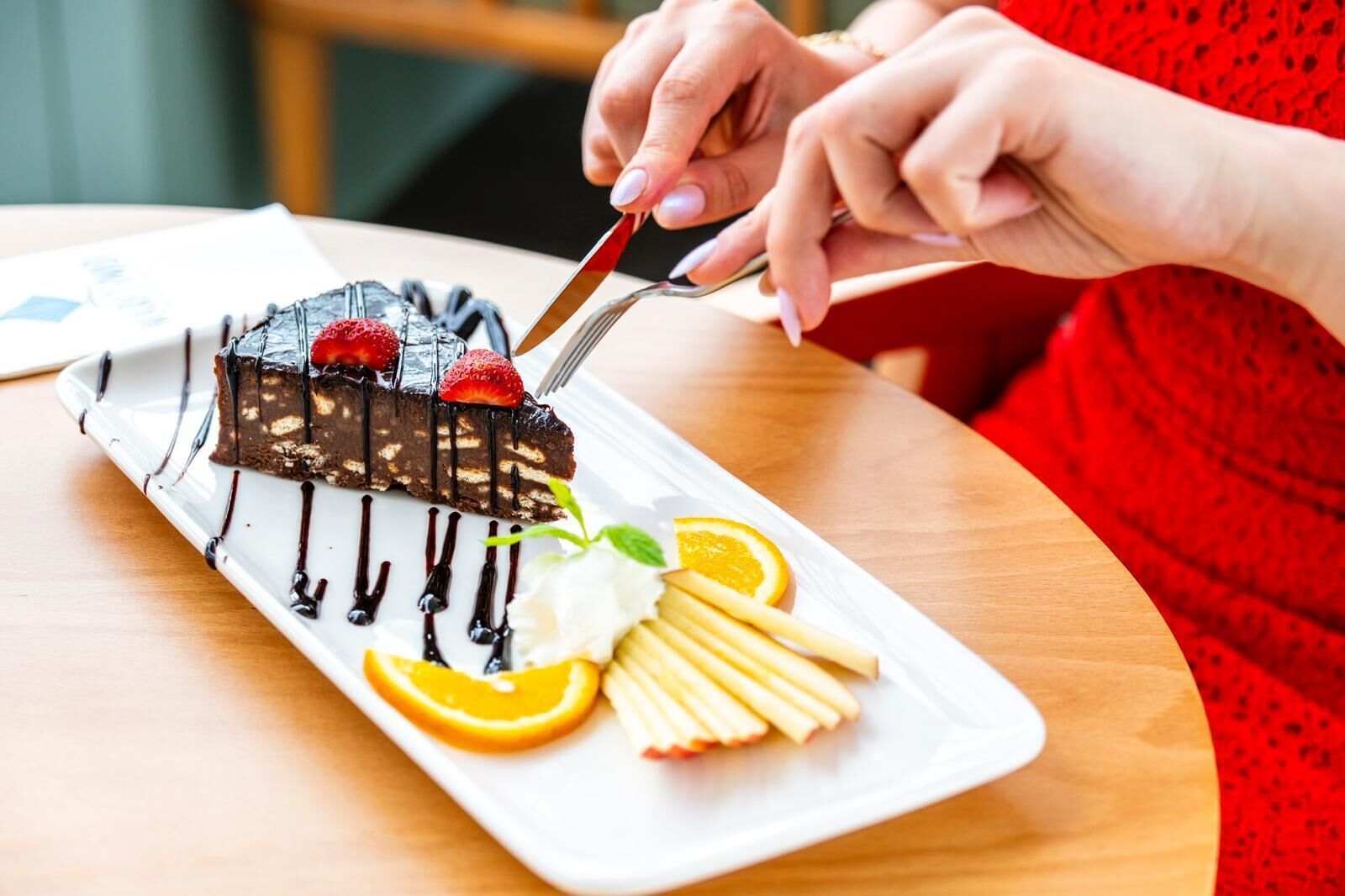 Um prato de sobremesa com bolo de chocolate, morangos, chantilly, fatias de laranja e palitos de wafer.