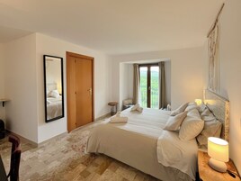 Quarto de hotel com uma cama grande, espelho, janela com cortinas, mesa de cabeceira com abajur e vista para o exterior.