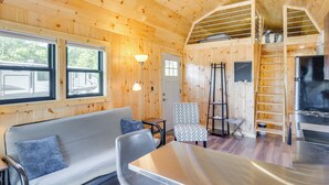 Interior acolhedor de uma cabana com sofá, cadeiras, mesa, lareira e um mezanino.
