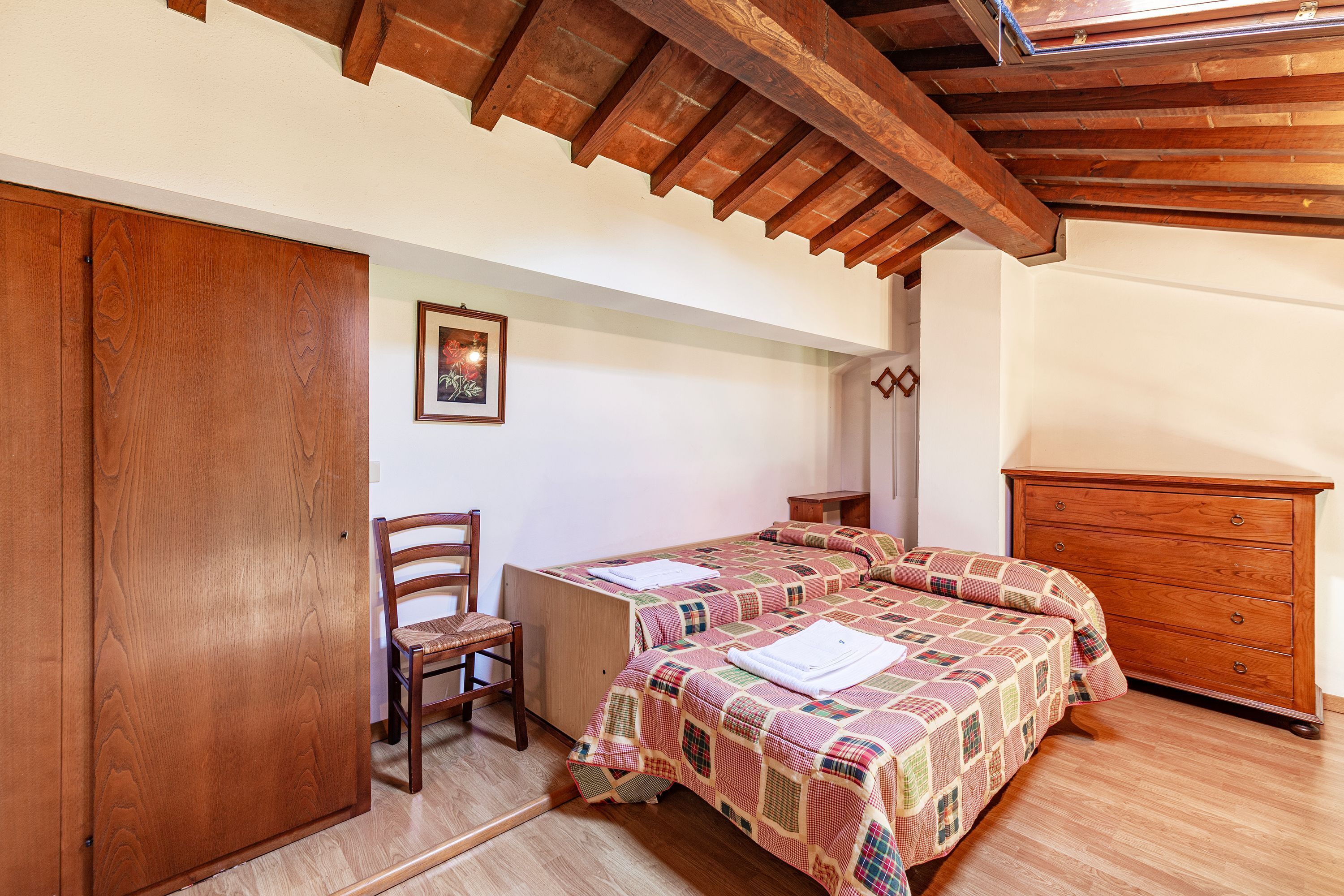 Quarto com duas camas, guarda-roupa de madeira, escrivaninha e uma cadeira.