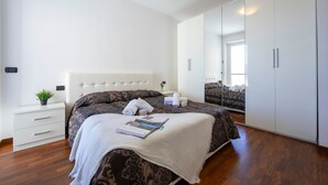 Quarto com cama grande, mesa de cabeceira com abajur, criado-mudo e guarda-roupa, além de espelho.