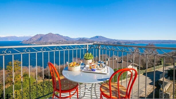 Uma varanda com mesa posta para dois, com vista panorâmica para montanhas e um corpo de água.